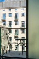 Uma varanda com duas cadeiras e uma mesa, com vista para um edifício com várias janelas e varandas.