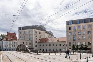 Trilhos de bonde com uma ponte, edifícios com várias janelas e uma passadeira para peões.