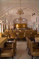 Uma ampla sala de jantar com pé direito alto, lustres e janelas em arco.