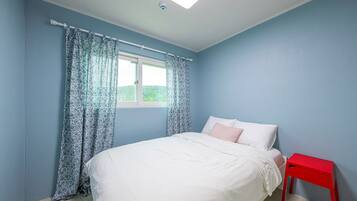 Quarto com uma cama, uma janela com cortinas e uma mesinha de cabeceira vermelha.