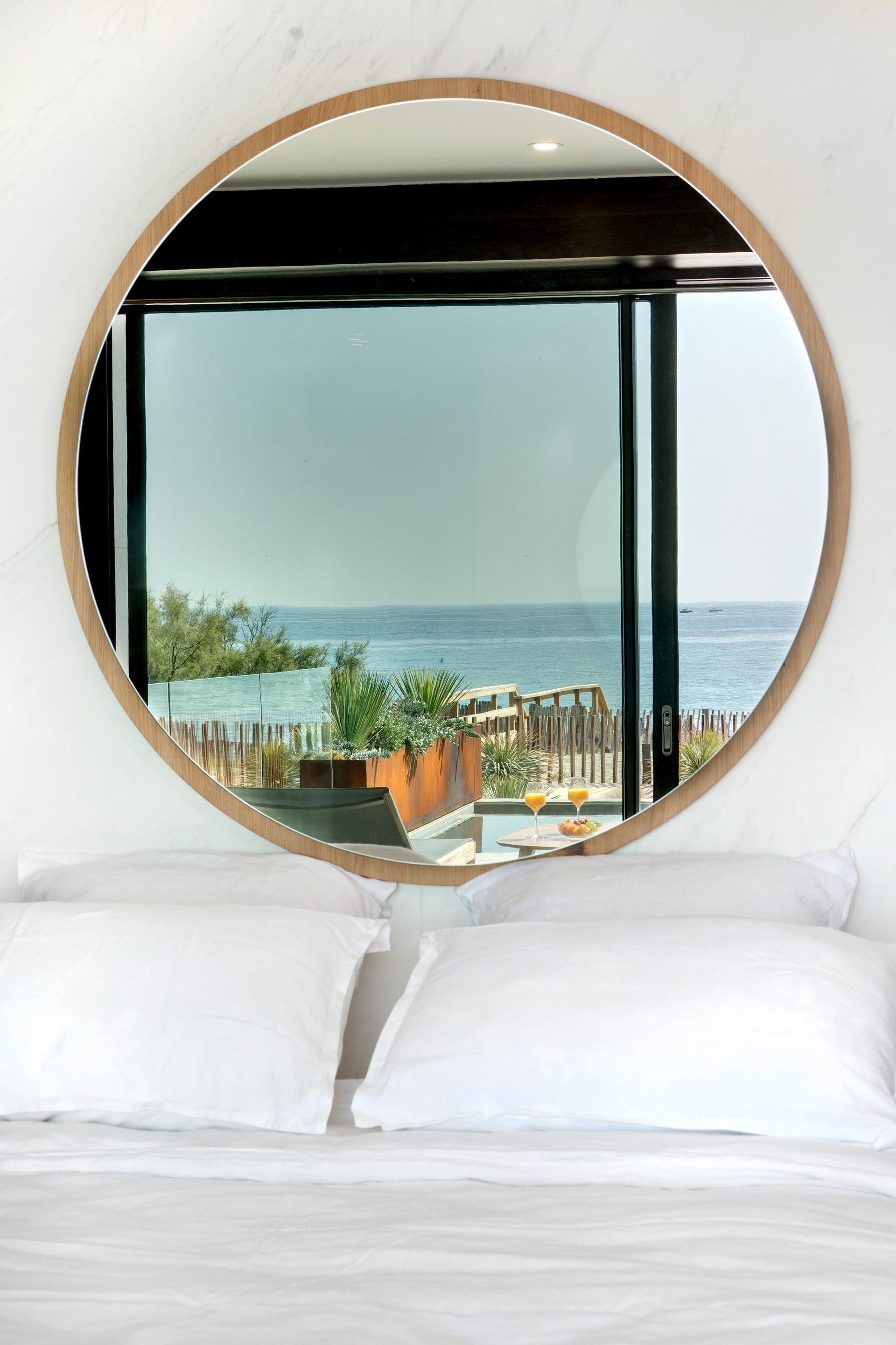 Quarto com um espelho redondo grande refletindo vista do mar e um deck de madeira.