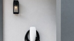Uma estação de carregamento Tesla fixada na parede, com cabo e luminária de parede.