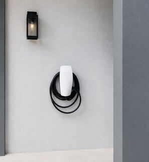 Uma estação de carregamento Tesla fixada na parede, com cabo e luminária de parede.