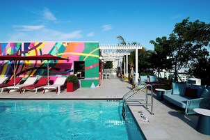 Uma área de piscina com espreguiçadeiras, um mural colorido e uma pérgula branca.