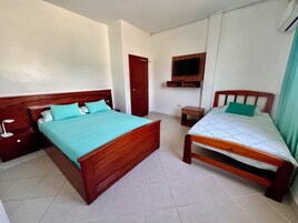 Quarto com duas camas de madeira, uma mesa de cabeceira de madeira, televisão montada na parede e uma porta.