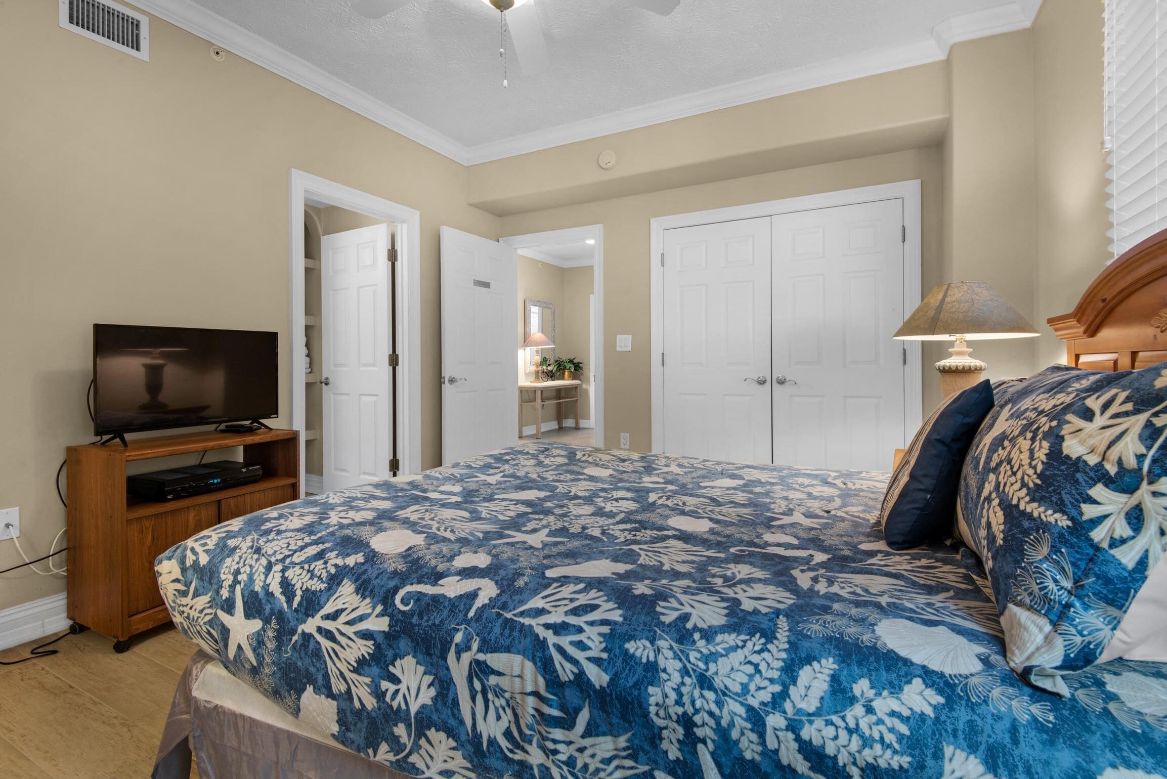 Quarto com uma cama grande, televisão sobre um suporte de madeira e ventilador de teto.
