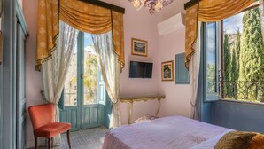 Um quarto com cama, uma cadeira, uma mesa e uma janela com cortinas.