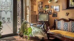 Um quarto antigo com uma televisão antiga, uma scooter e um sofá de madeira com almofadas estampadas.