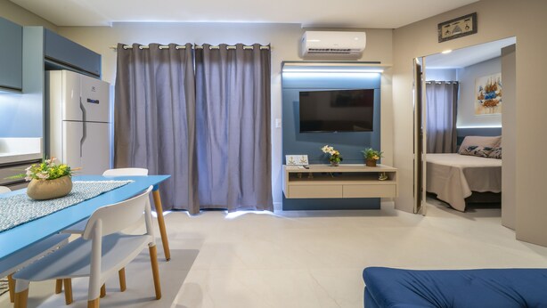 Um espaço compacto com área de refeições, TV fixada na parede, cama e pequena cozinha.