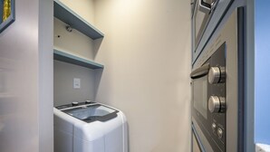 Uma lavanderia compacta com máquina de lavar e secadora frontais, forno embutido e uma pequena prateleira sobre a secadora.