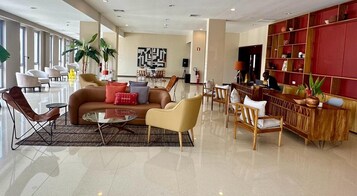 Um hall amplo com um sofá de couro, poltronas, uma mesa de centro e um balcão de recepção.