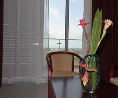 Quarto com uma janela grande, uma cadeira, uma mesa e um vaso com flores.