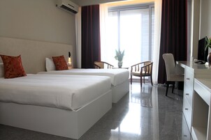 Quarto de hotel com duas camas, uma mesa, uma cadeira e um vaso de planta.