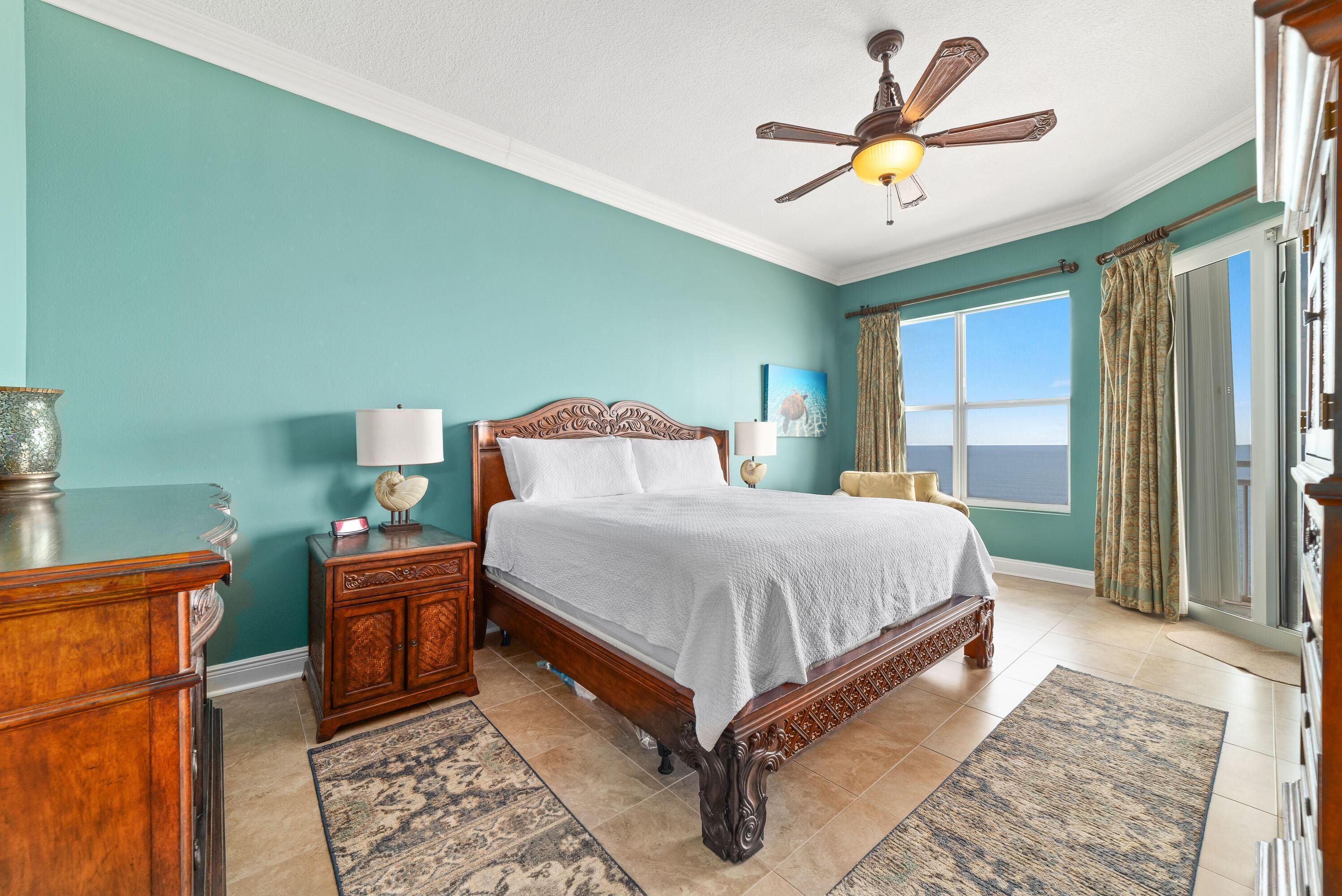 Quarto com cama grande, mesa de cabeceira de madeira e ventoinha no teto.