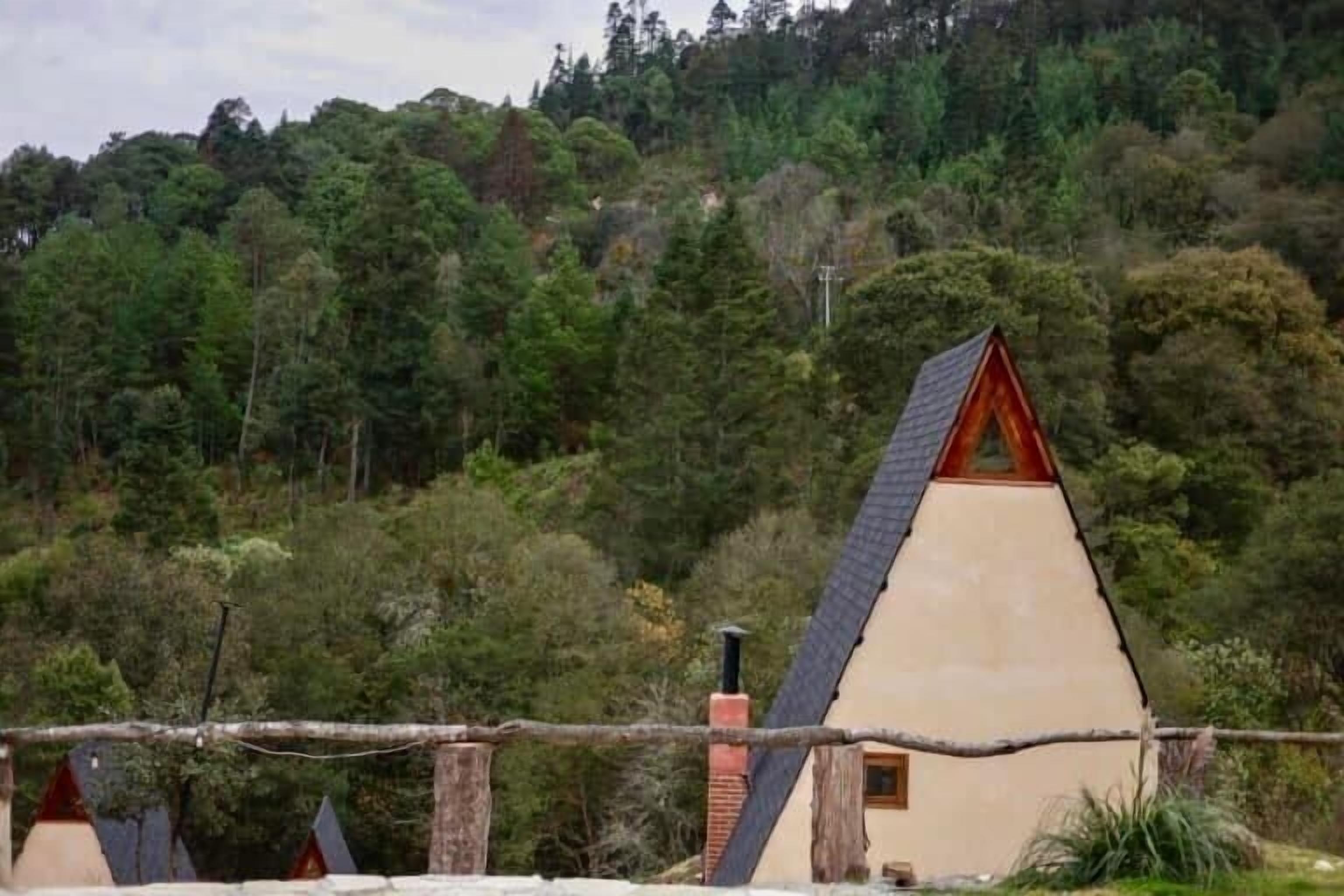 Um pequeno edifício com telhado triangular e fachada bege, cercado por uma área florestal natural.