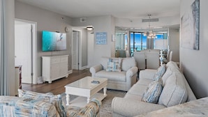 Uma sala de estar ampla com uma televisão de tela plana grande, um conjunto de sofás confortáveis e um espaço de jantar com vista para o oceano.