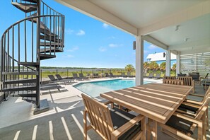 Uma área à beira da piscina com escada em espiral, espreguiçadeiras e uma mesa de madeira.