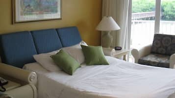 Quarto de hotel com cama, poltrona, abajur e janela com vista para o verde.