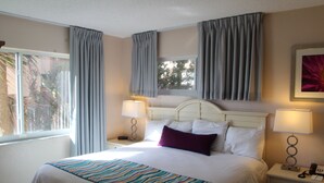 Quarto de hotel com uma cama grande, duas mesas de cabeceira, uma janela com cortinas e um quadro na parede.