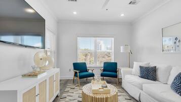 Uma sala de estar moderna com um sofá branco, duas poltronas azuis, uma mesa de centro redonda de madeira e um armário branco com portas de vime.
