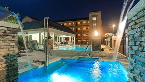 Piscina com cascata, rodeada por espreguiçadeiras e um edifício ao fundo.