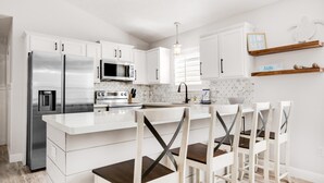 Uma cozinha moderna com armários brancos, eletrodomésticos de aço inoxidável e uma ilha central com banquetas.