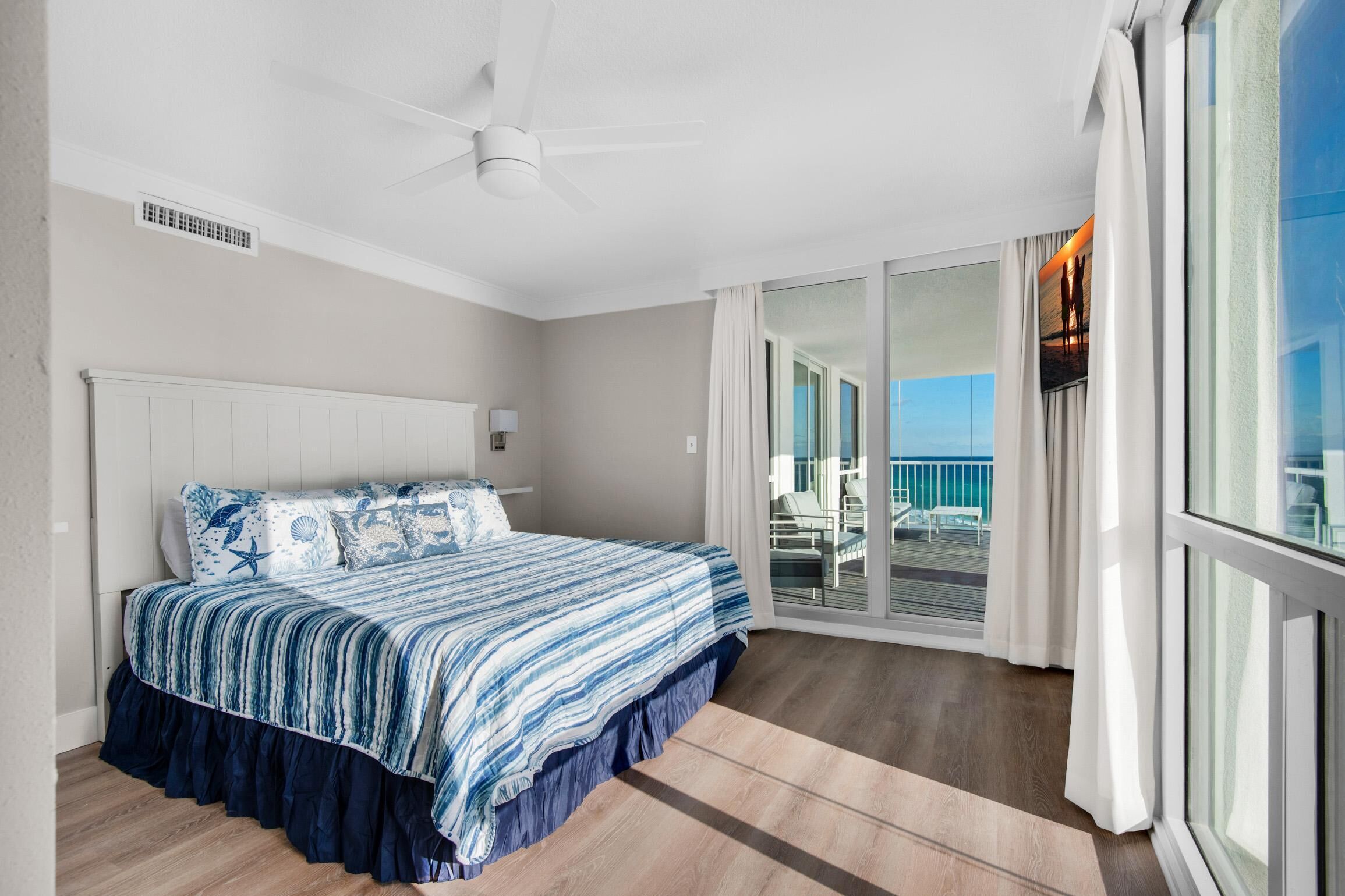 Quarto com cama, ventoinha no teto, janela com cortinas e vista para o exterior.
