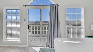 Quarto com uma cama grande, uma varanda com vista e duas janelas com persianas.