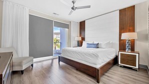 Quarto de hotel moderno com uma cama grande, um ventilador de teto, mesa de cabeceira com abajur e vista para o exterior.