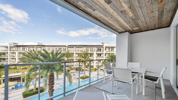 Varanda com vista para uma piscina e palmeiras, móveis brancos e teto de madeira.