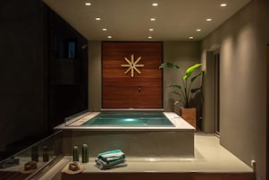 Uma área de spa moderna com parede de madeira, uma luz em formato de estrela brilhante, uma banheira de hidromassagem em vidro e uma planta.