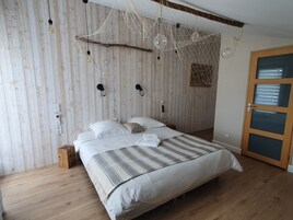 Quarto com parede de madeira, cama com roupa de cama branca, manta listrada e piso de madeira.