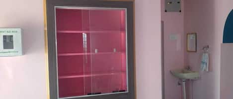 Um quarto com paredes cor-de-rosa, um armário de madeira e uma janela com moldura vermelha.