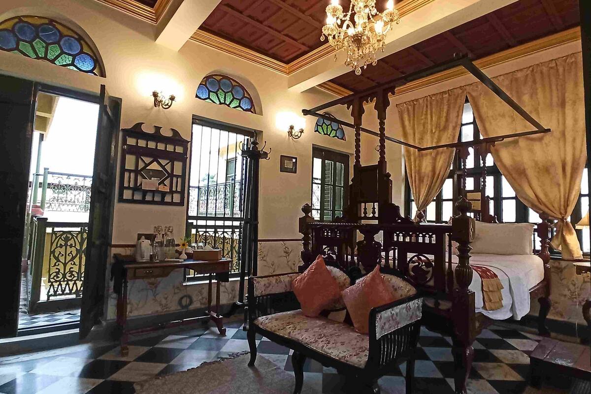 Quarto tradicional com cama de dossel, uma cadeira de madeira e chão xadrez.