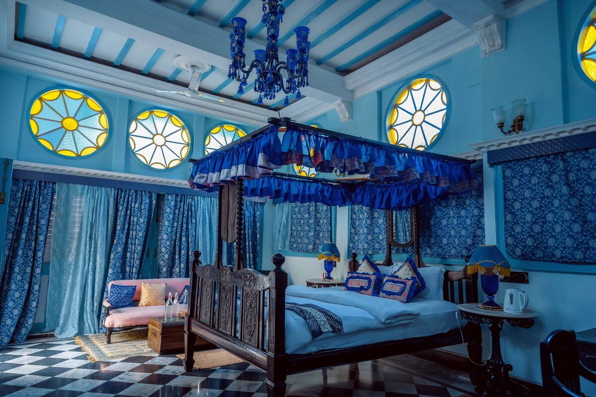 Quarto com uma cama de dossel, um sofá, uma mesinha de cabeceira com abajur e uma cadeira.