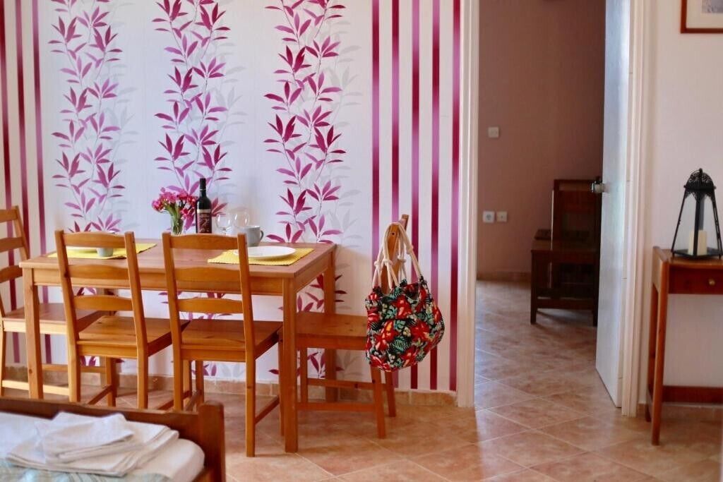 Uma sala de jantar com mesa e cadeiras de madeira, papel de parede listrado e uma bolsa pendurada na parede.