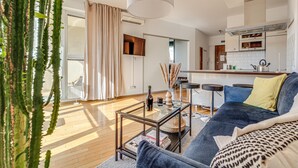 Uma sala de estar moderna com um sofá, mesa de centro e área de refeições, com uma cozinha ao fundo.