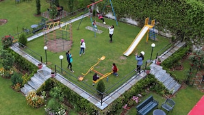 Um parquinho com balanços, escorregadores e estruturas de escalada, cercado por jardins bem cuidados e caminhos.