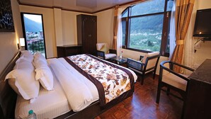 Quarto de hotel com cama, escrivaninha, cadeira, televisão e janela com vista para as montanhas.