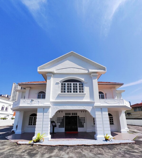 Um edifício branco em estilo colonial com uma entrada central, duas alas e telhado em telhas.