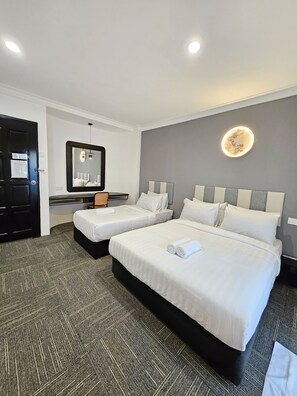 Quarto de hotel com duas camas, um espelho grande, uma escrivaninha e um ponto de luz fixado na parede.