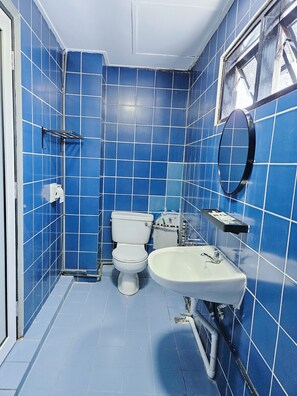 Um banheiro com paredes azulejadas em azul, vaso sanitário branco, pia e espelho.