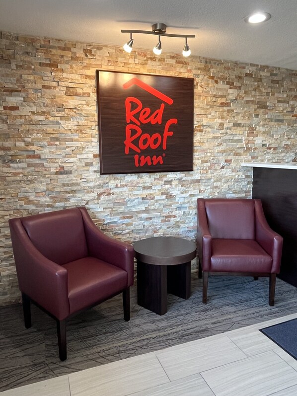 Área de recepção do Red Roof Inn com parede de pedra ao fundo, dois poltronas de couro, uma pequena mesa redonda e um lustre.