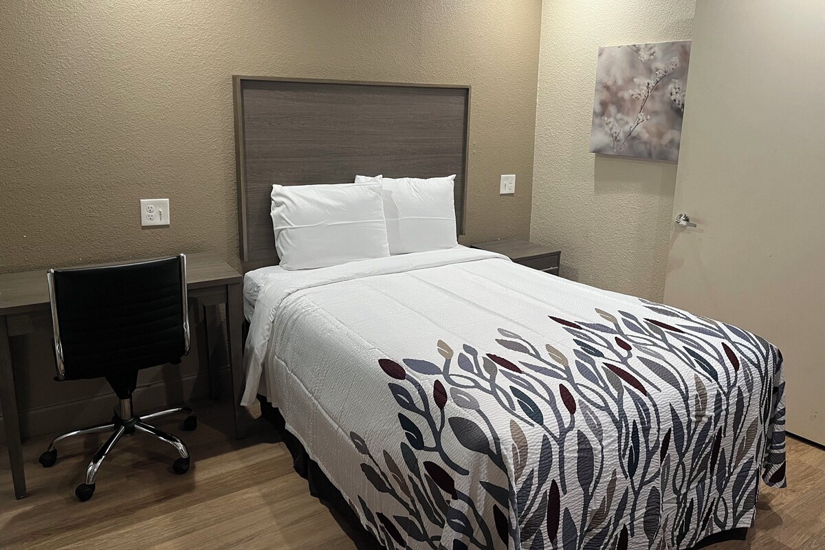 Quarto de hotel com cama, escrivaninha e cadeira.