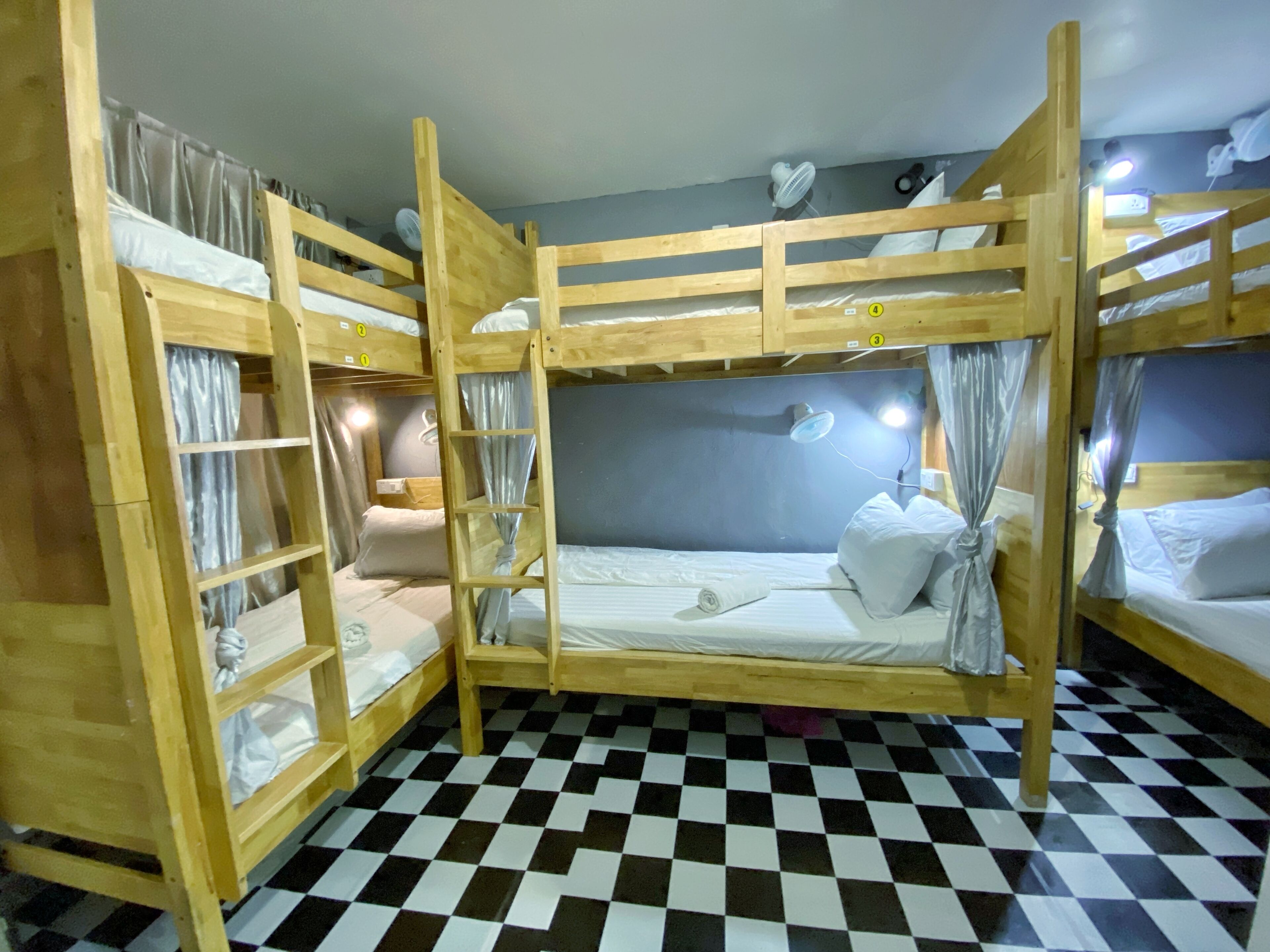Quarto com beliches, chão quadriculado, escada e ventilador de teto.