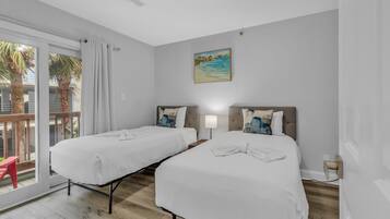 Quarto de hotel com duas camas, varanda com uma cadeira vermelha e um quadro com cena de praia.