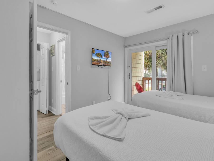 Quarto de hotel com duas camas, uma televisão na parede e vista para palmeiras pela janela.