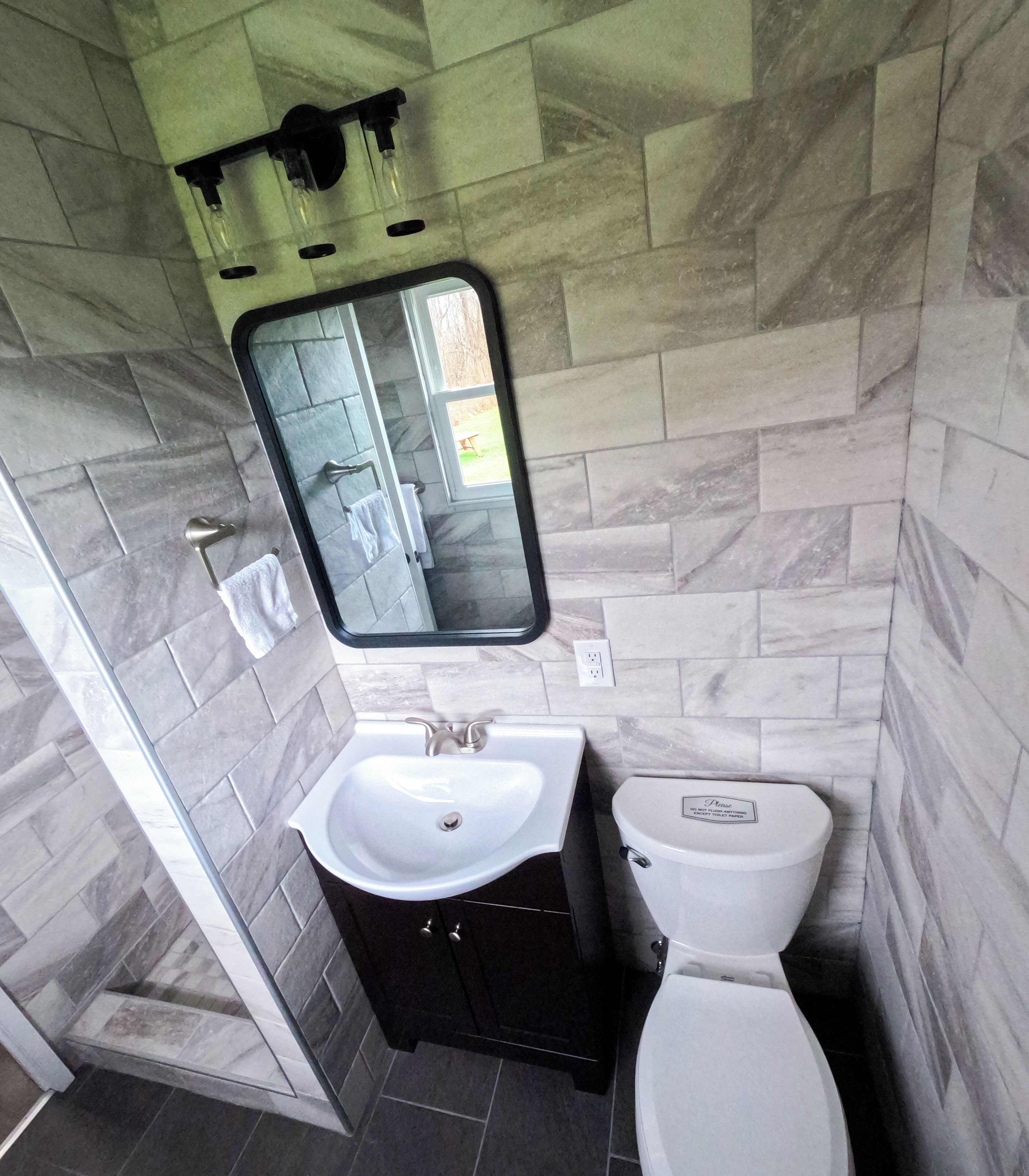 Casa de banho com lavatório branco, sanita e espelho sobre o lavatório. As paredes estão revestidas a azulejos em padrão herringbone.