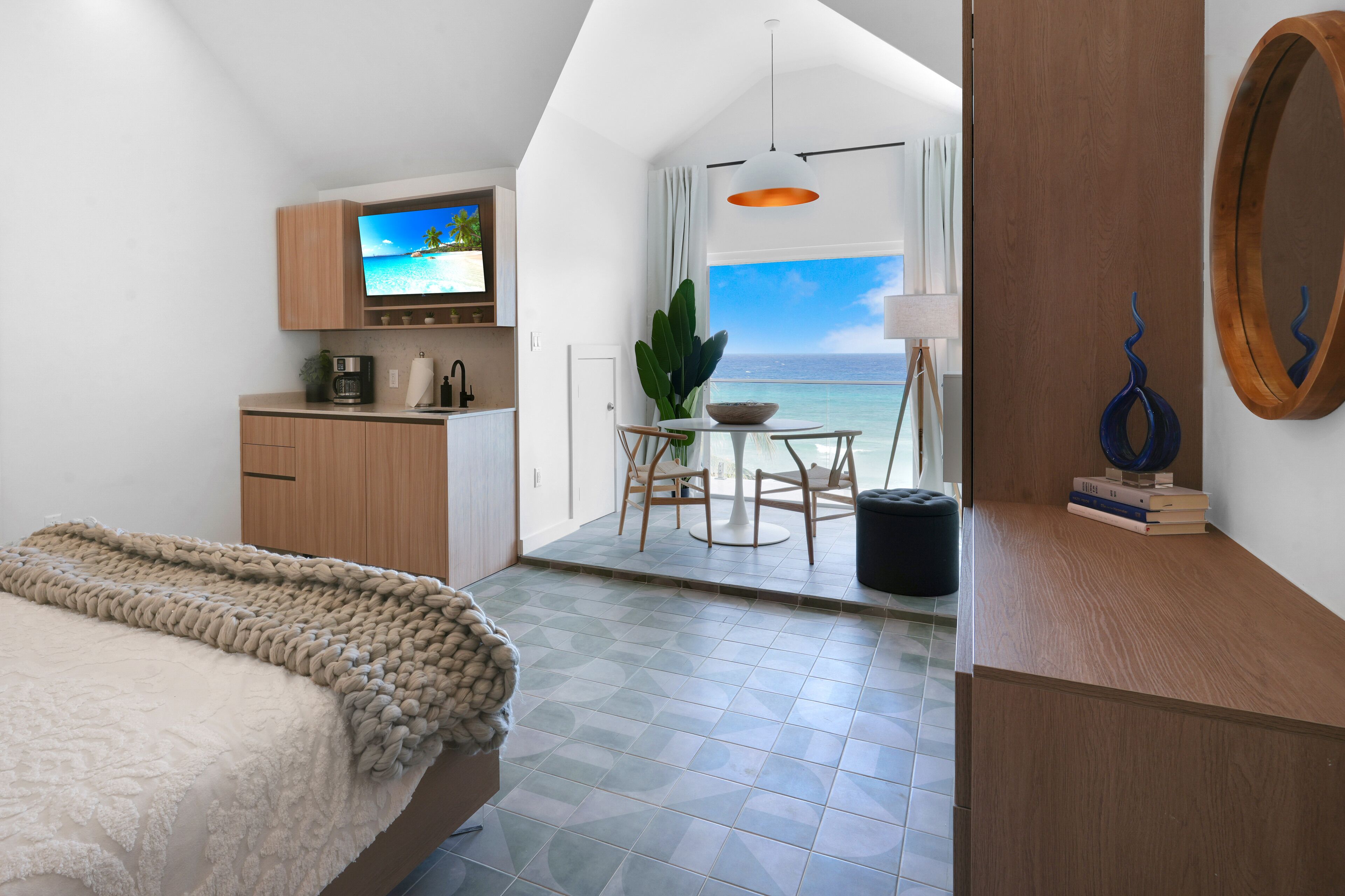 Quarto moderno com cama, cozinha compacta e varanda com vista para o oceano.