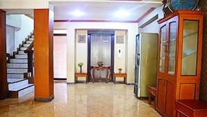 Um corredor amplo com piso de mármore, escada de madeira à esquerda, uma porta no final e um armário de madeira com portas de vidro à direita.